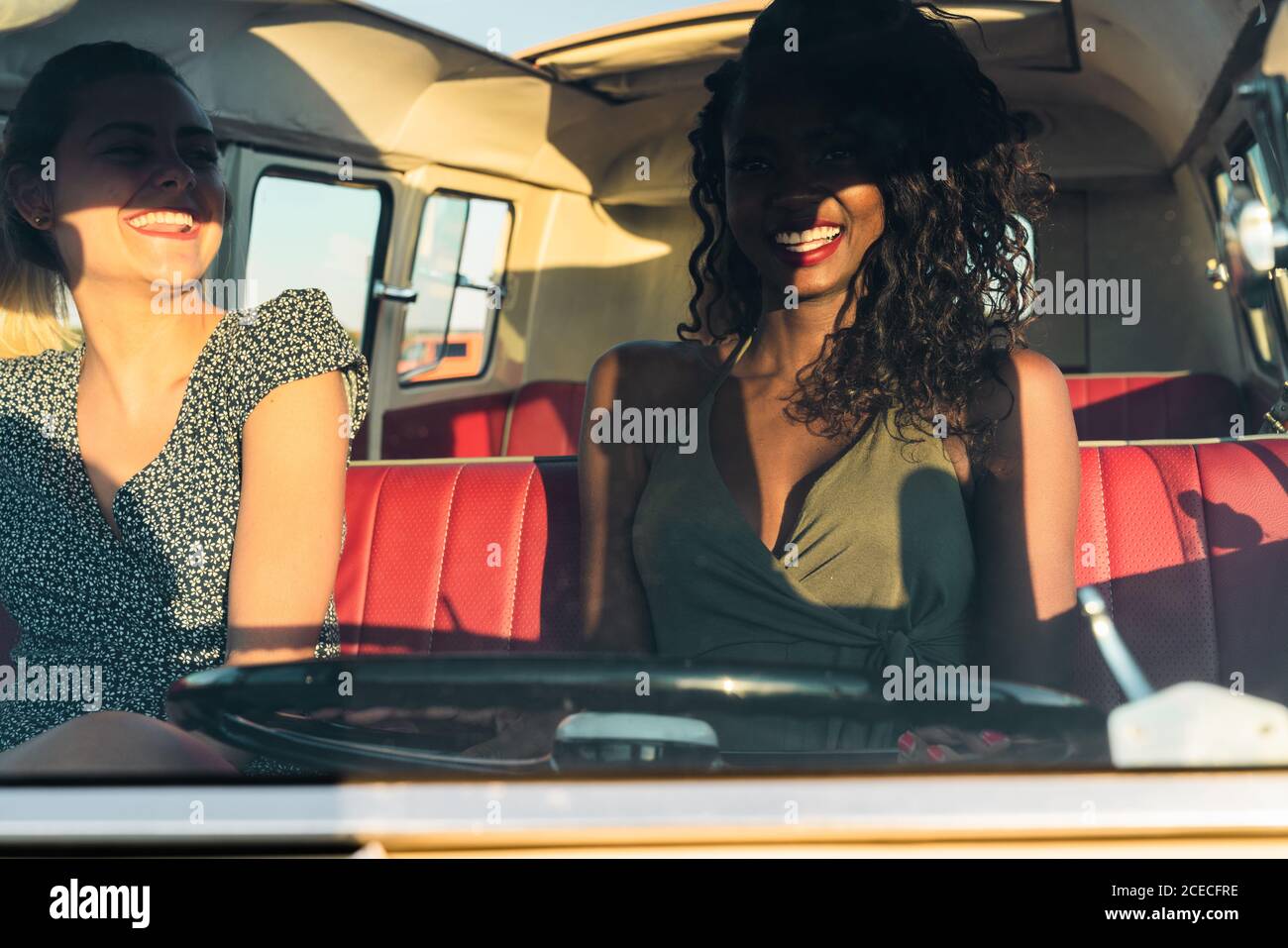 two young women sitting inside vintage van and smiling while traveling ...