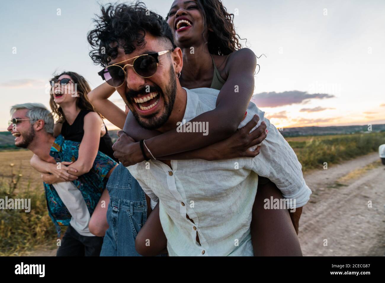 Two men giving piggyback ride to women and running along countryside ...