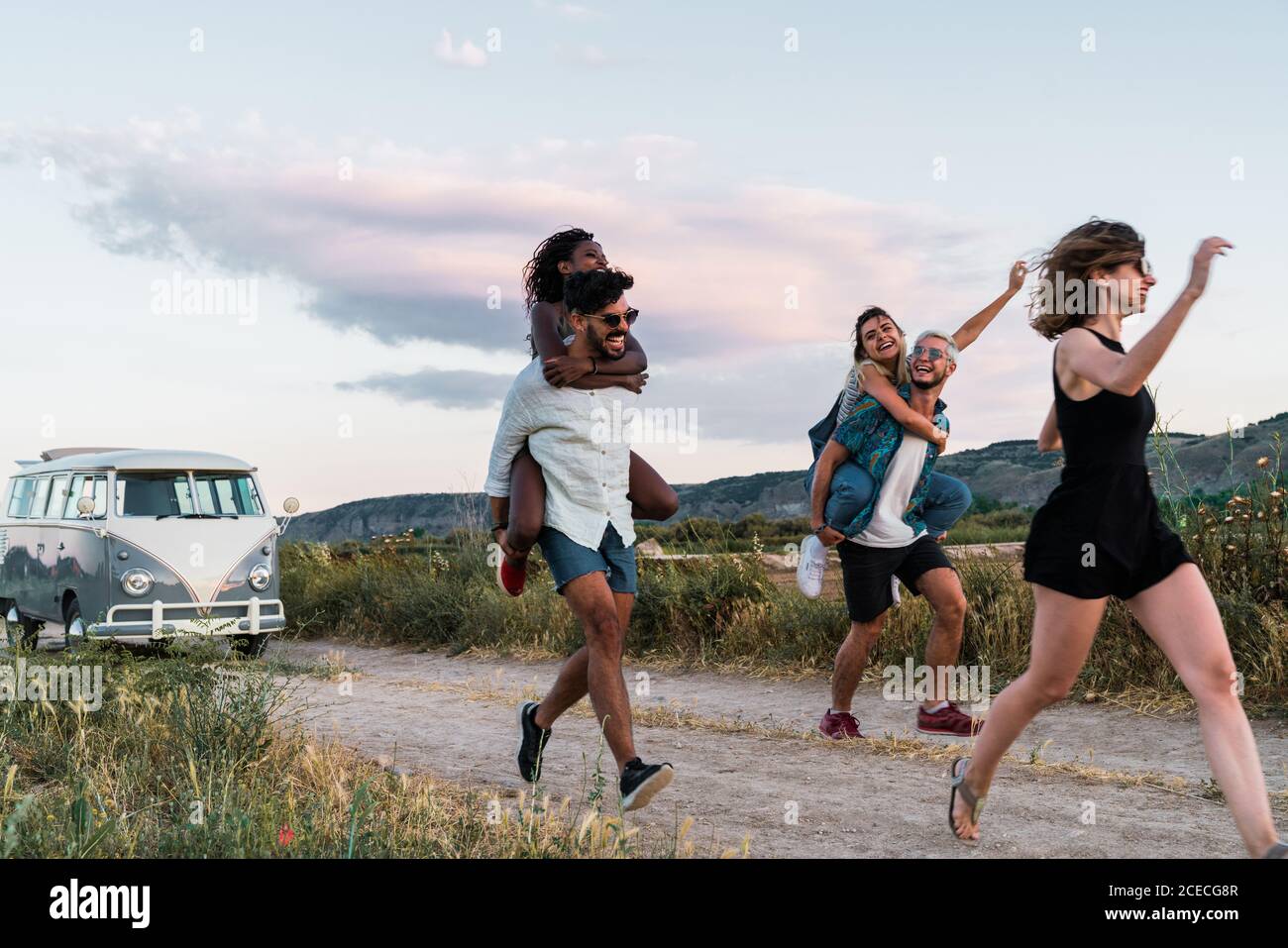 Two men giving piggyback ride to women and running along countryside ...