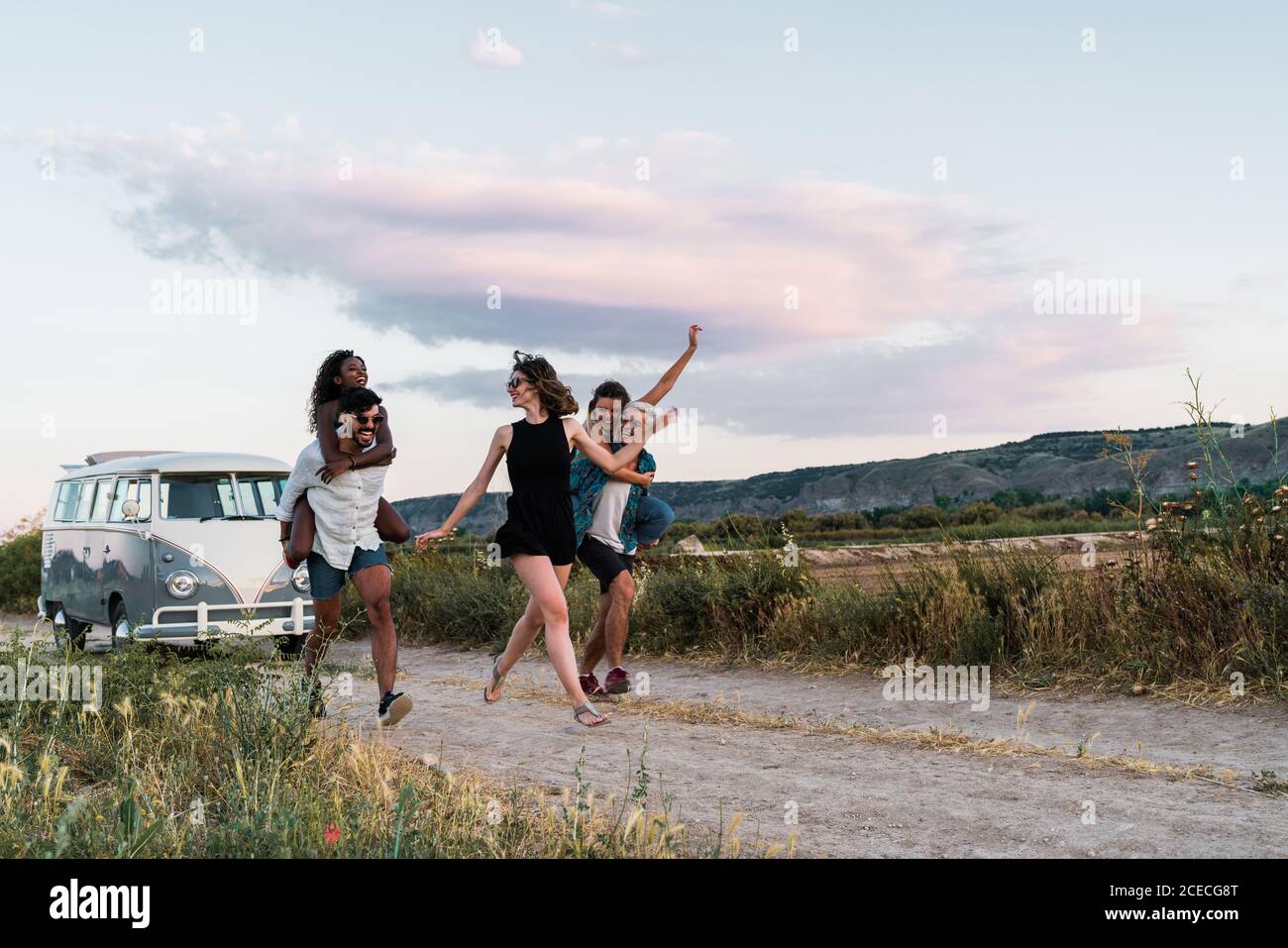 Two men giving piggyback ride to women and running along countryside ...