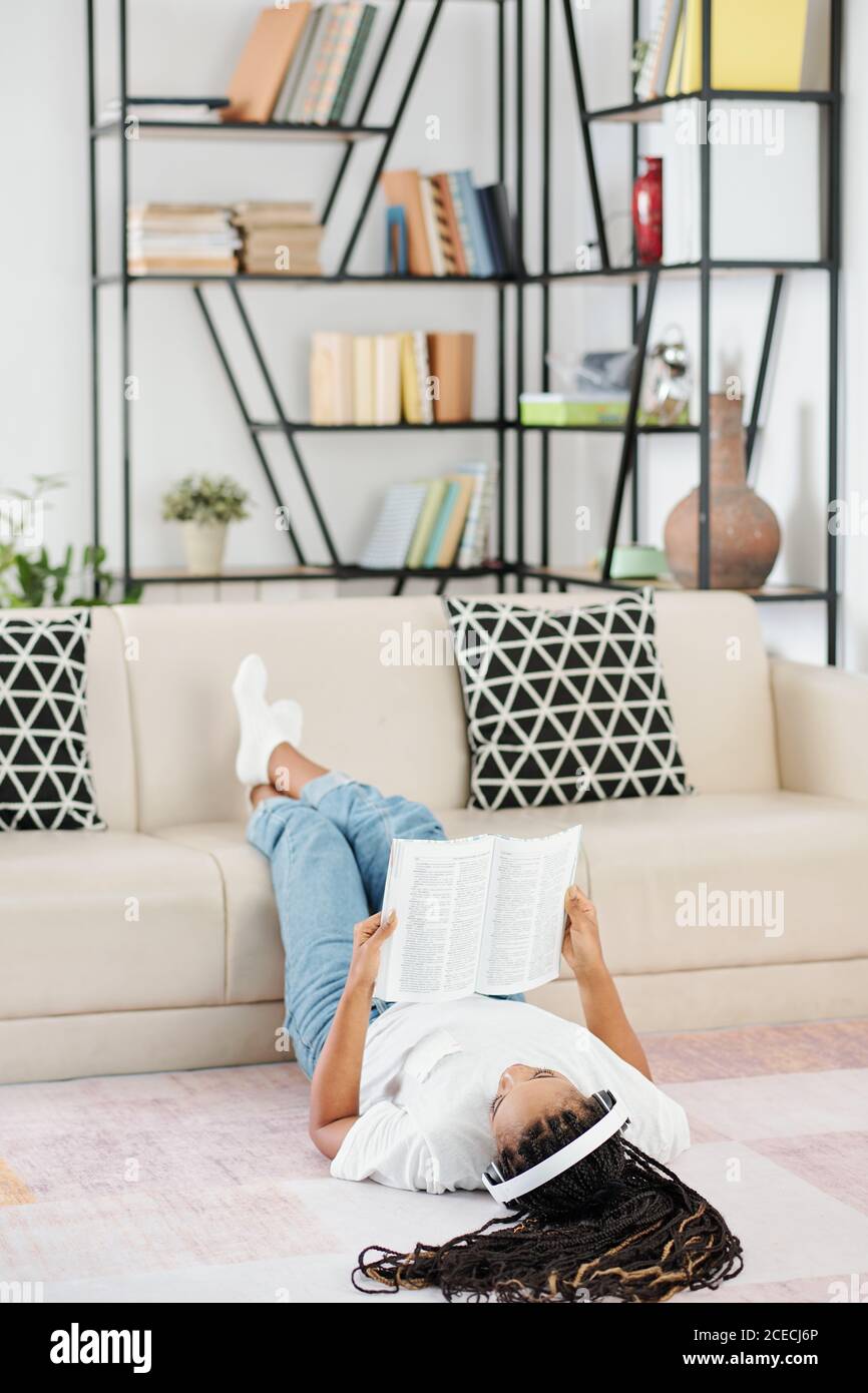 Young woman with dreadlocks lying on the floor with feet on sofa and ...