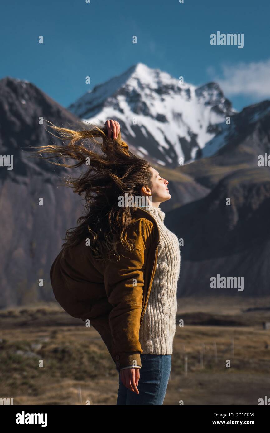 Side view of Woman with hair flying in wind standing with mountains on ...