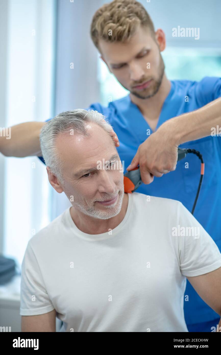 Bearded doctor performing ultrasound neck treatment on mature patient ...