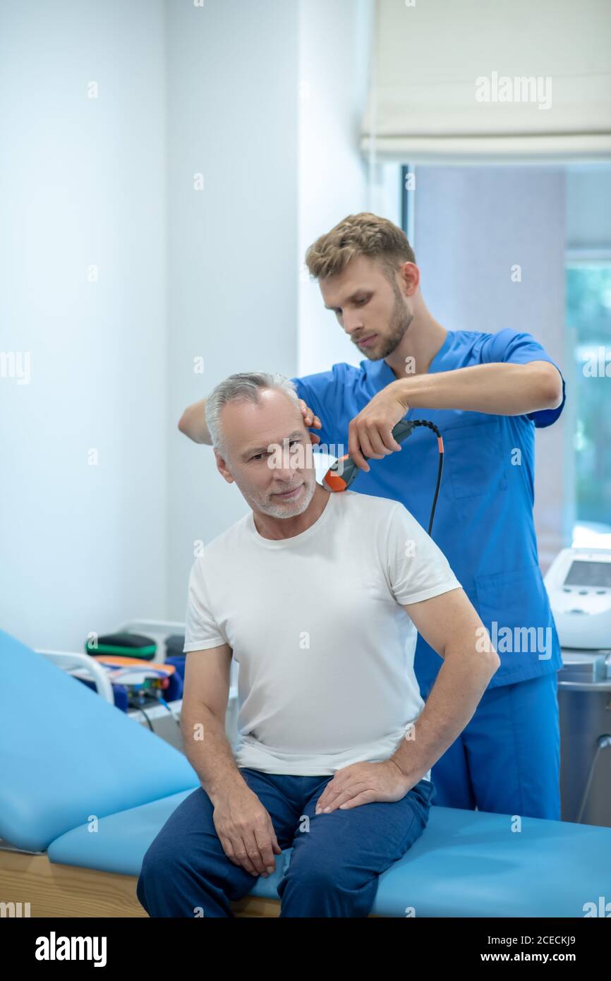 Bearded doctor performing ultrasound neck treatment on mature patient ...