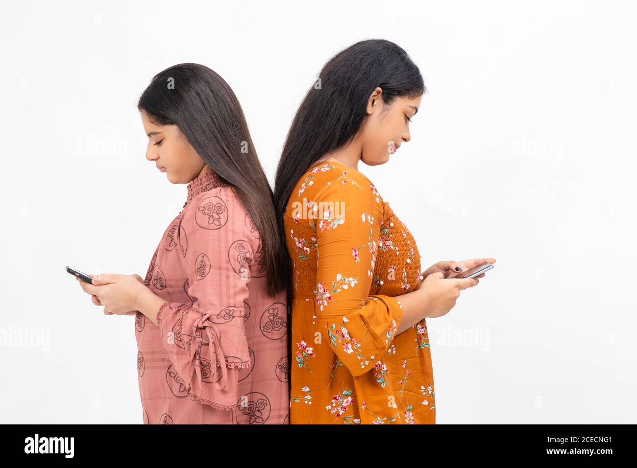 Two young teenager Indian girls busy on their smart phones, standing ...