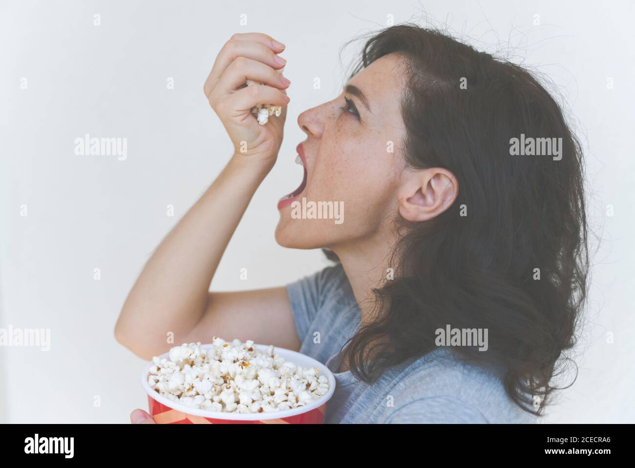 Attractive young woman pouring popcorn in mouth holding big bucket ...
