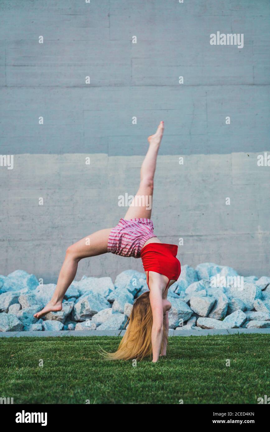 Side view of faceless young female doing handstand on grass near ...