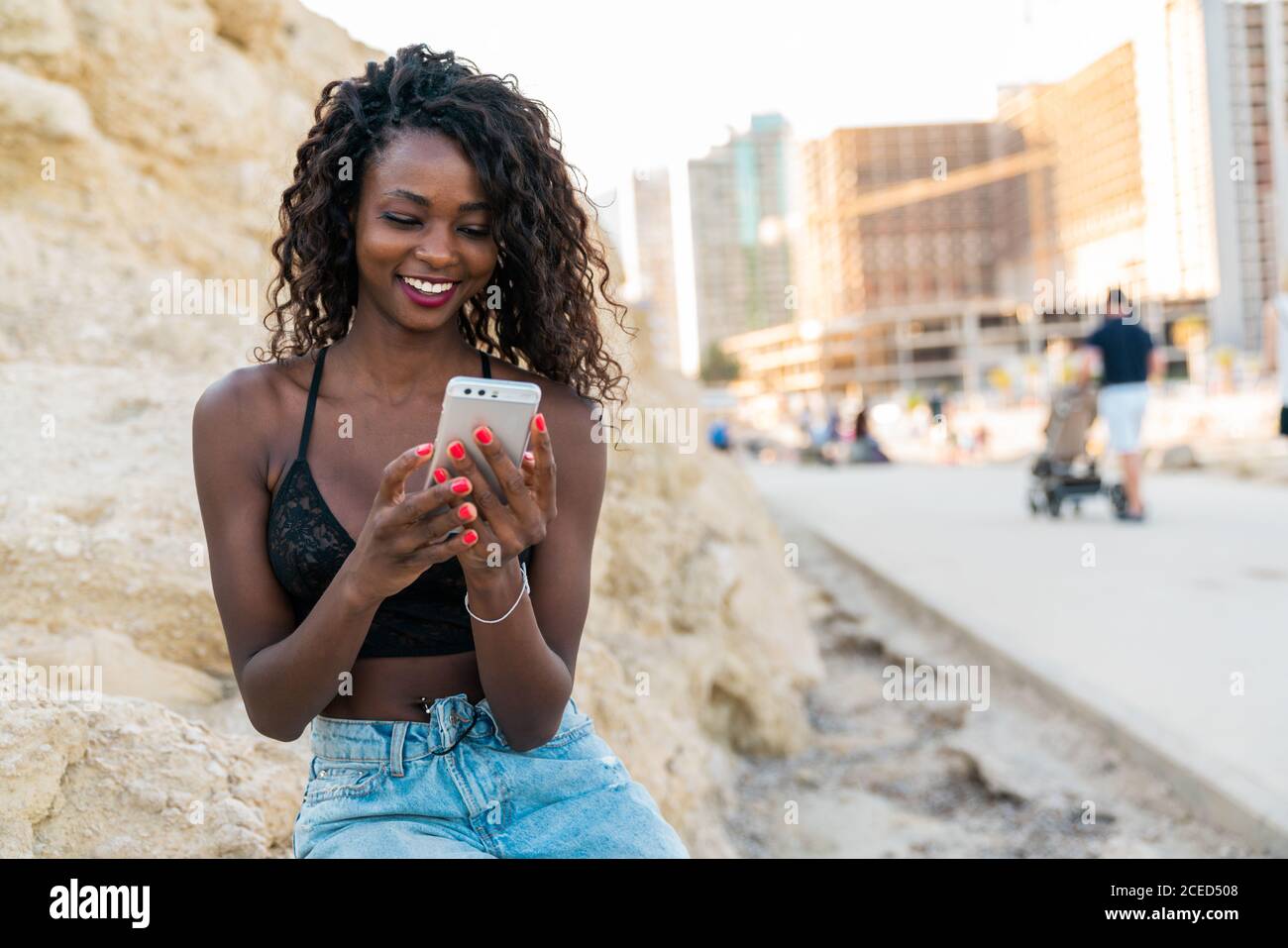 Cheerful pretty black Woman using phone outside Stock Photo - Alamy