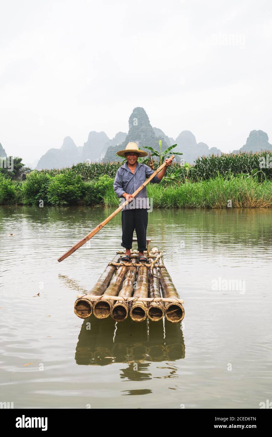 Smiling Asian elderly man in straw hat approaching standing on bamboo ...