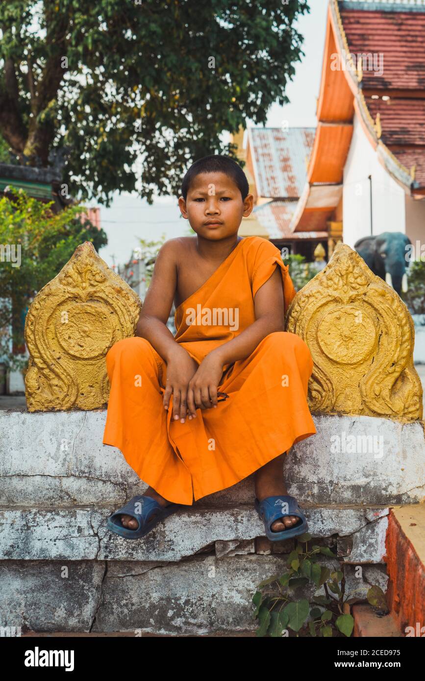 Little Asian monk boy in orange clothes looking at camera and sitting ...
