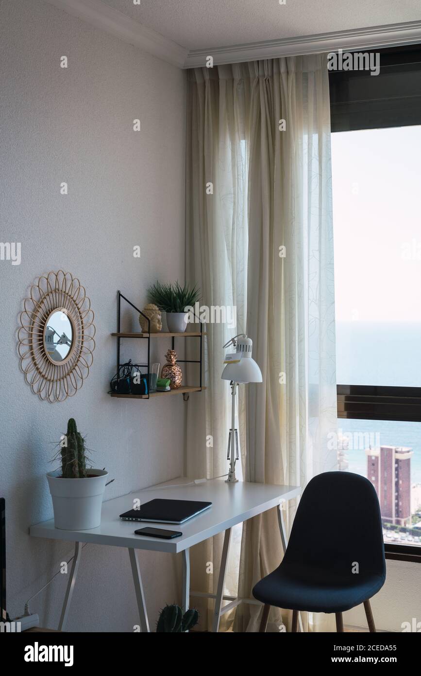 Various stuff standing on shelf and desk near huge window in cozy light ...