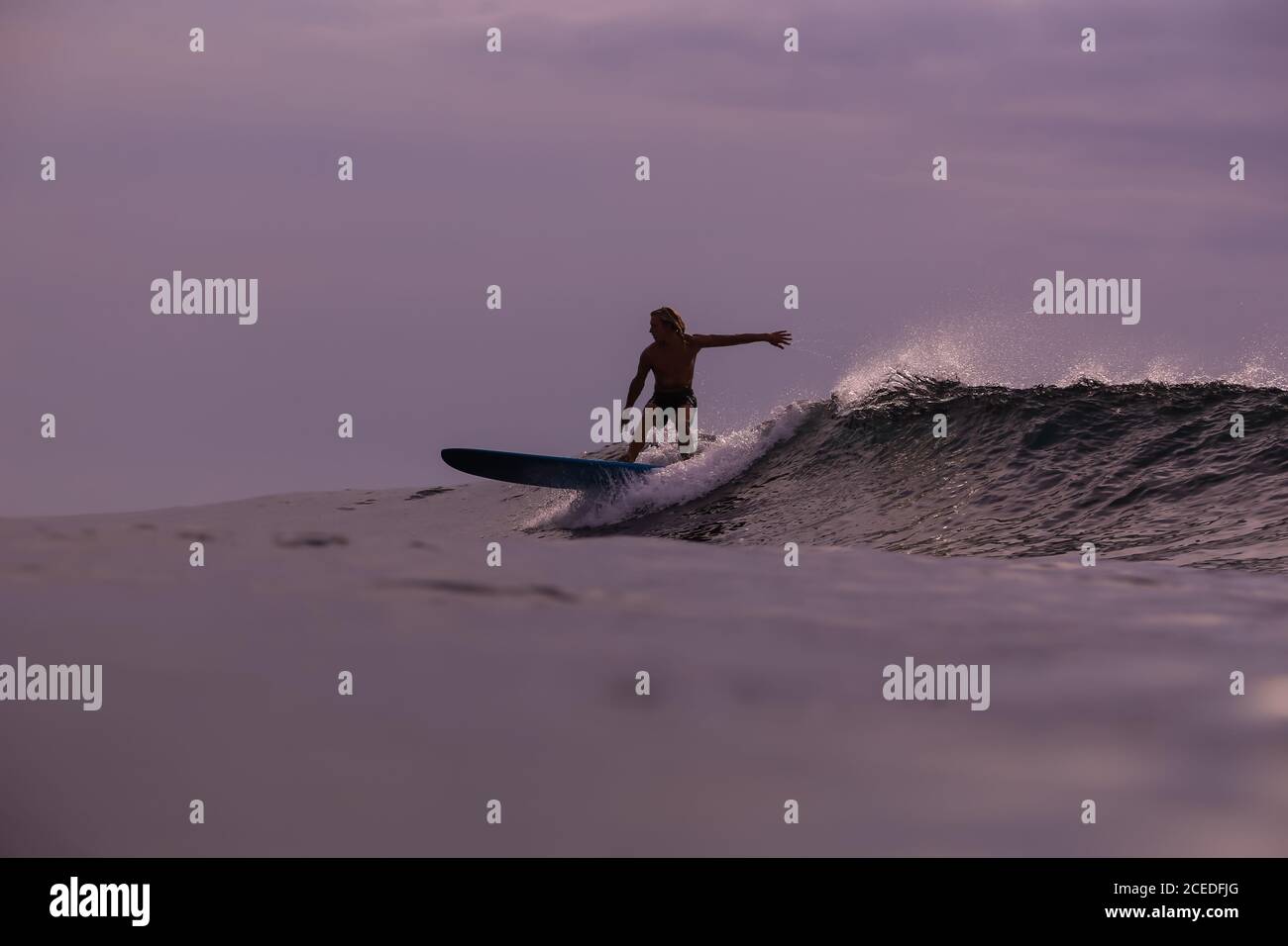Male surfing between waving water of sea with splashes and cloudy sky ...