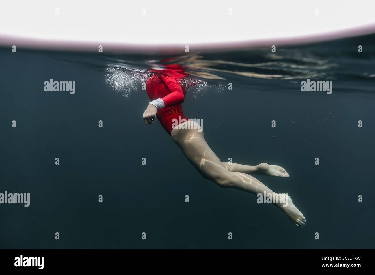 Side view of female in red swimsuit diving in blue water of sea on Bali ...