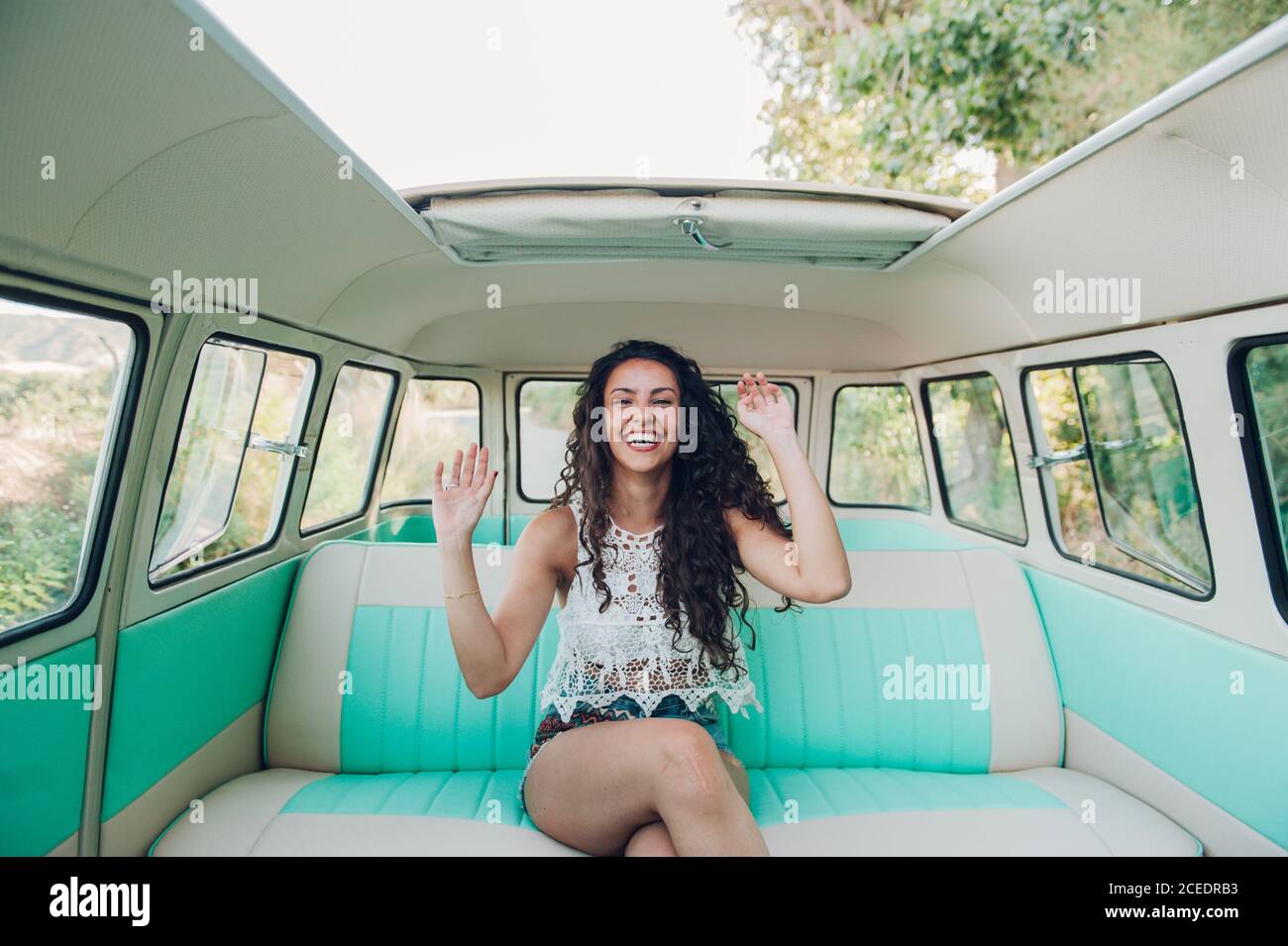 Attractive young brunette sitting on back seat of vintage van and ...