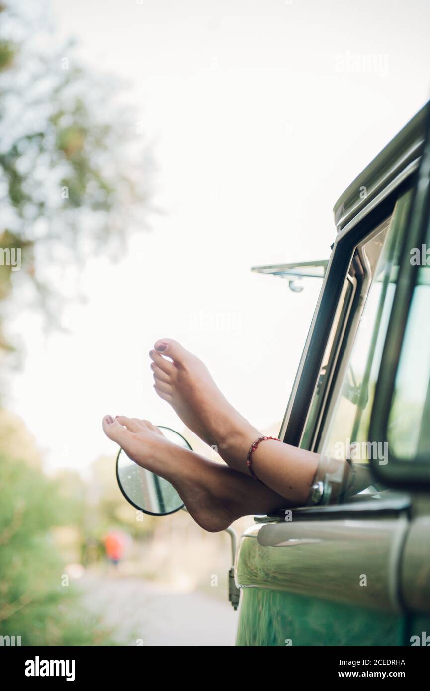Crop legs of barefoot lady hanging out from opened window of retro car ...