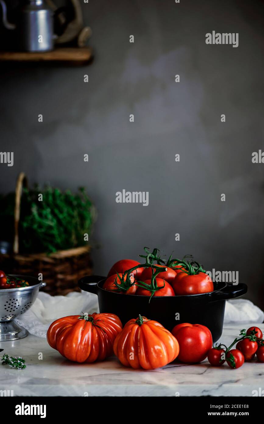 Big red ripe tomatoes of different forms in pot on table near grey wall ...