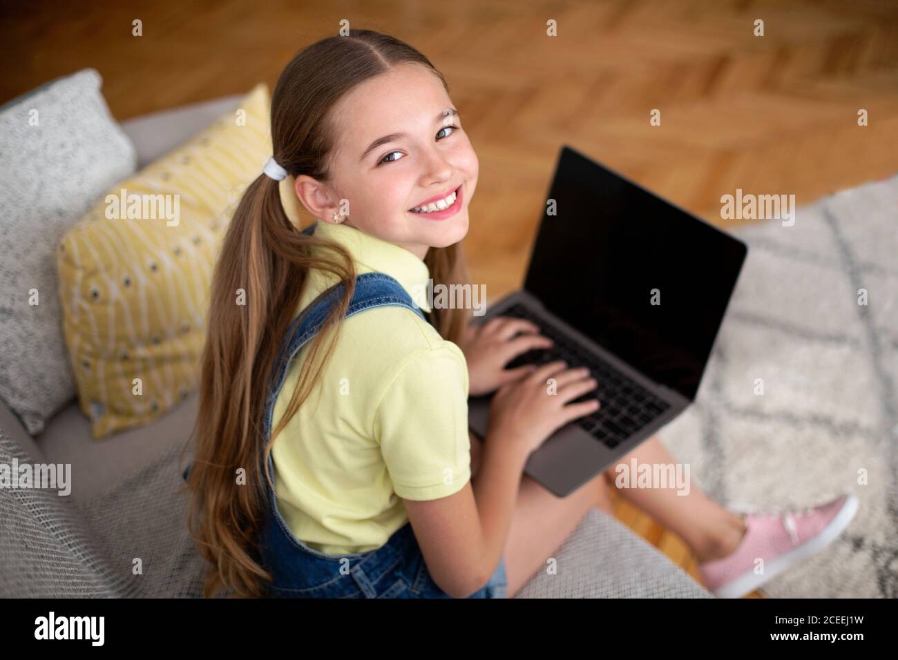 Girl using her laptop sitting on couch looking back Stock Photo - Alamy