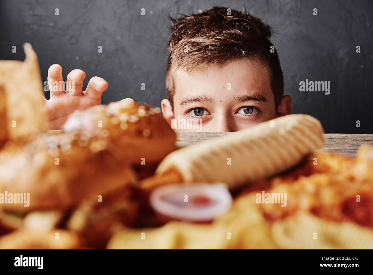 Hungry boy looks at tasty food and take hamburger from table. Unhealthy ...