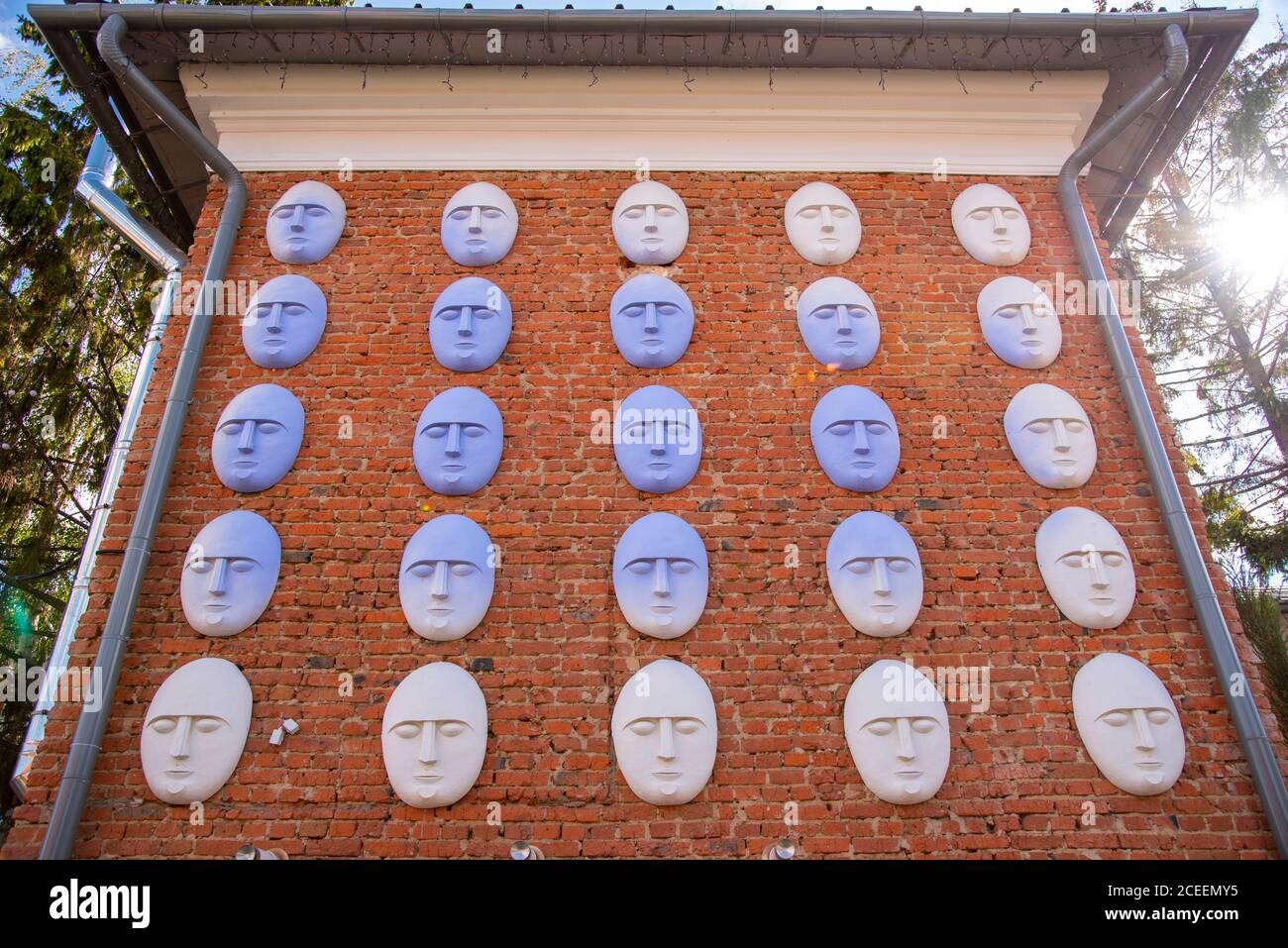 A brick wall hung with white and blue plaster masks. Contemporary art ...