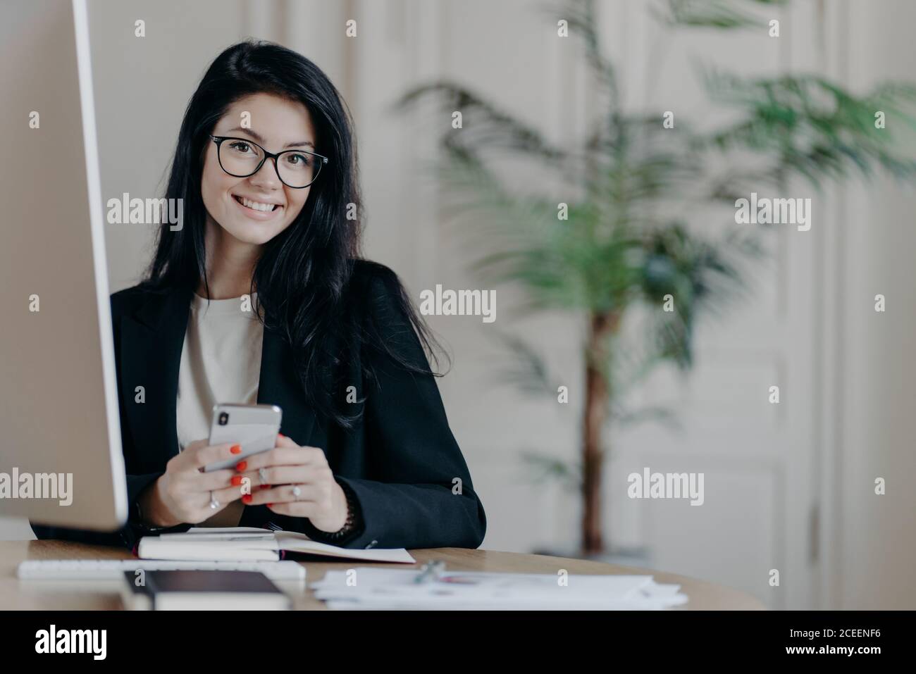 Happy female office worker in stylish black jacket browses smartphone ...