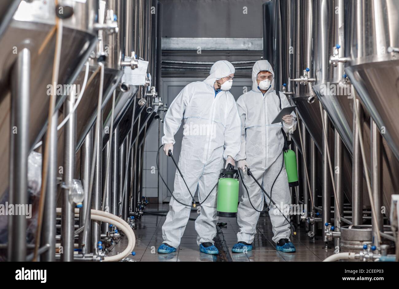 Guys in hazmat suits and masks disinfect brewery kettles at craft plant ...