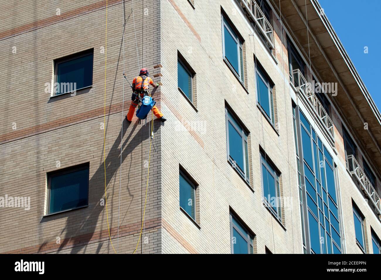 Man suspended by ropes hangs in the air on the corner of a block of ...