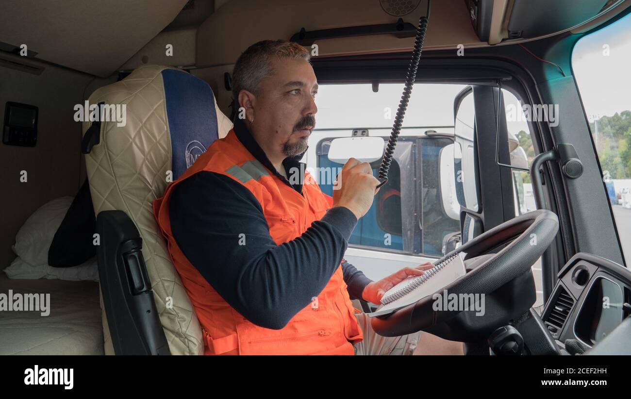 Male mechanic in an orange vest sitting on the driver's seat of a truck ...