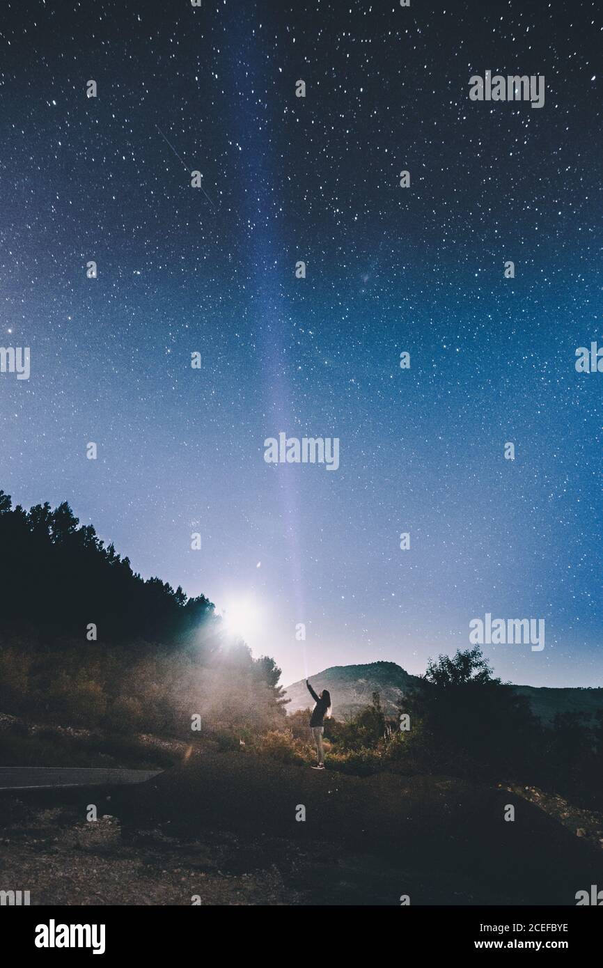 Side view at distance of Woman standing on roadside under blue starry ...