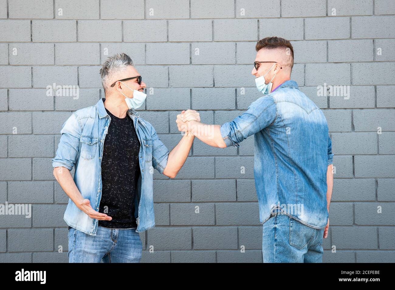 Friends with lowered protective masks doing greetings with handshake ...