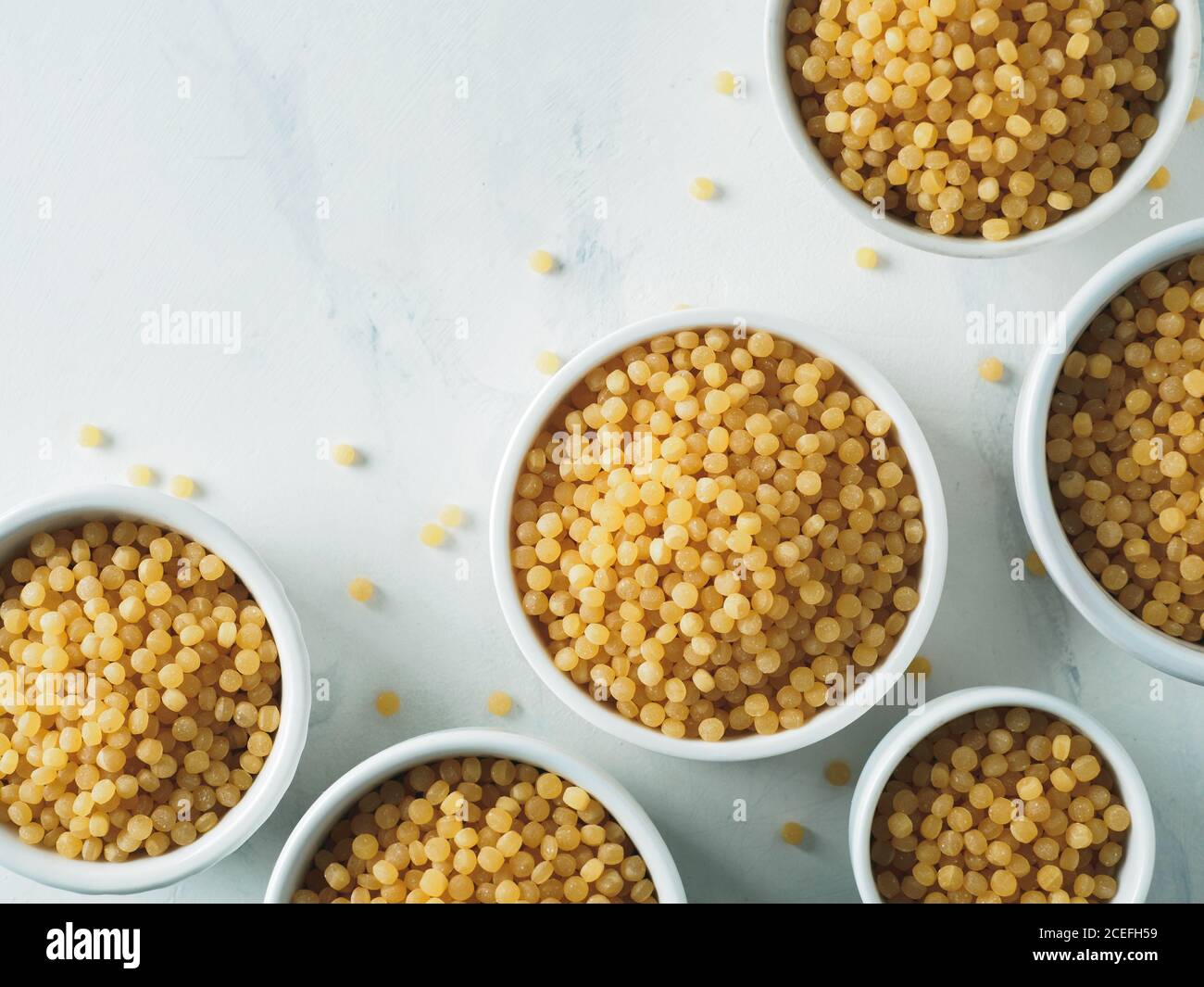 Top view of ptitim pasta in bowls on white marble tabletop. Ptitim or ...