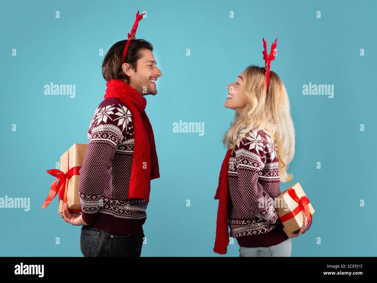 Side view of joyful couple hiding Christmas gifts behind their backs ...