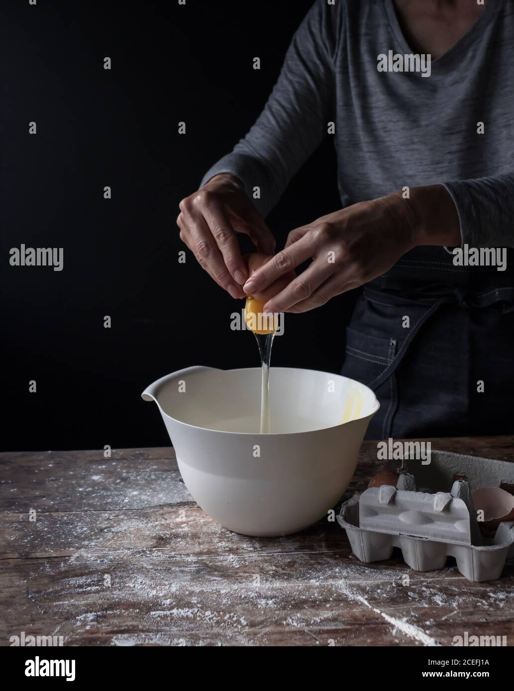 Crop human breaking egg in bowl on wooden table with flour on black ...