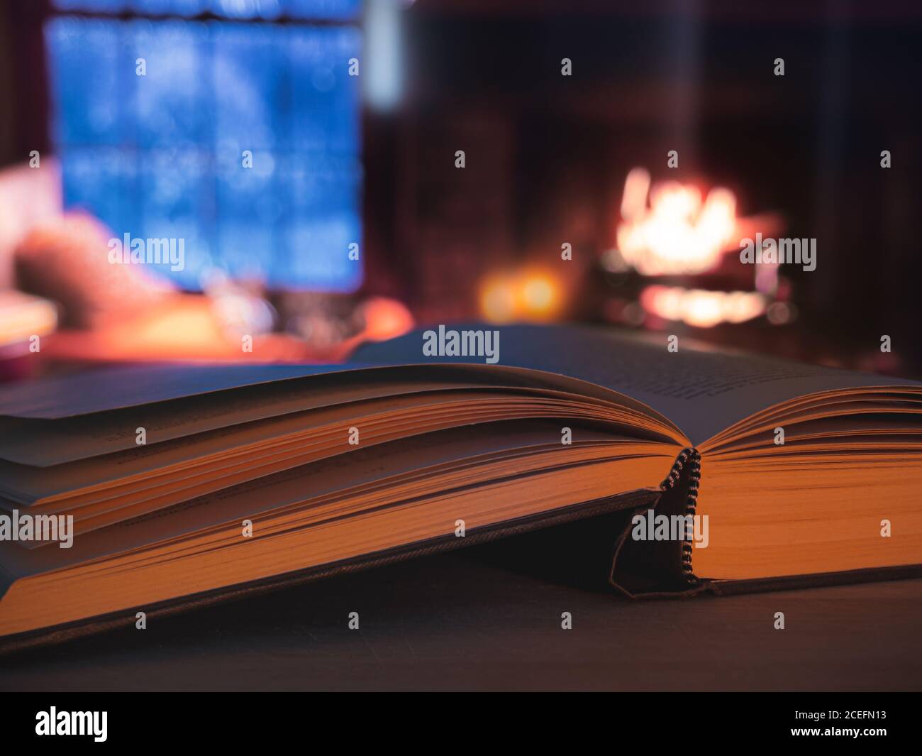 An open book on a wooden table in a log cabin lit by candles and a ...
