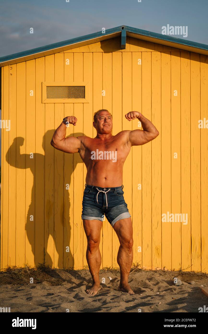 Muscular older man poses yellow background Stock Photo - Alamy