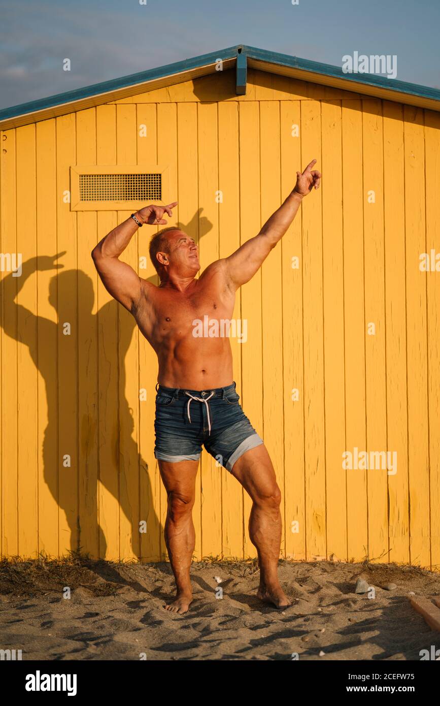Muscular older man poses yellow background Stock Photo - Alamy