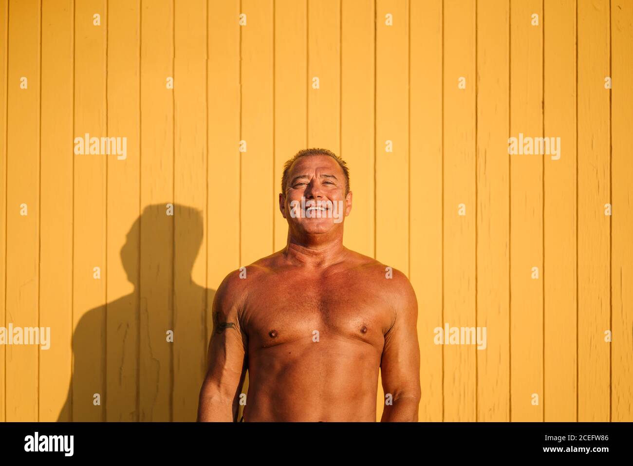 Muscular older man poses yellow background Stock Photo - Alamy