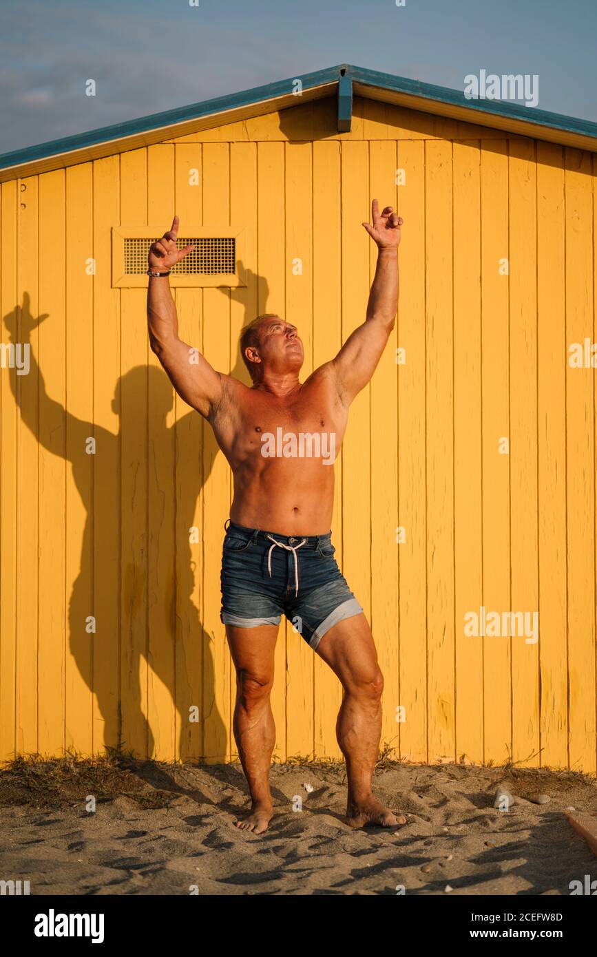 Muscular older man poses yellow background Stock Photo - Alamy