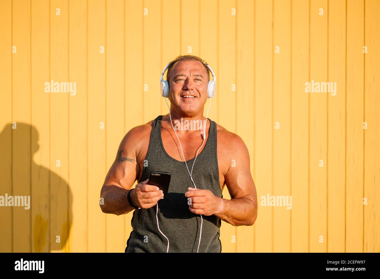Strong older man poses with headphones on yellow background Stock Photo ...