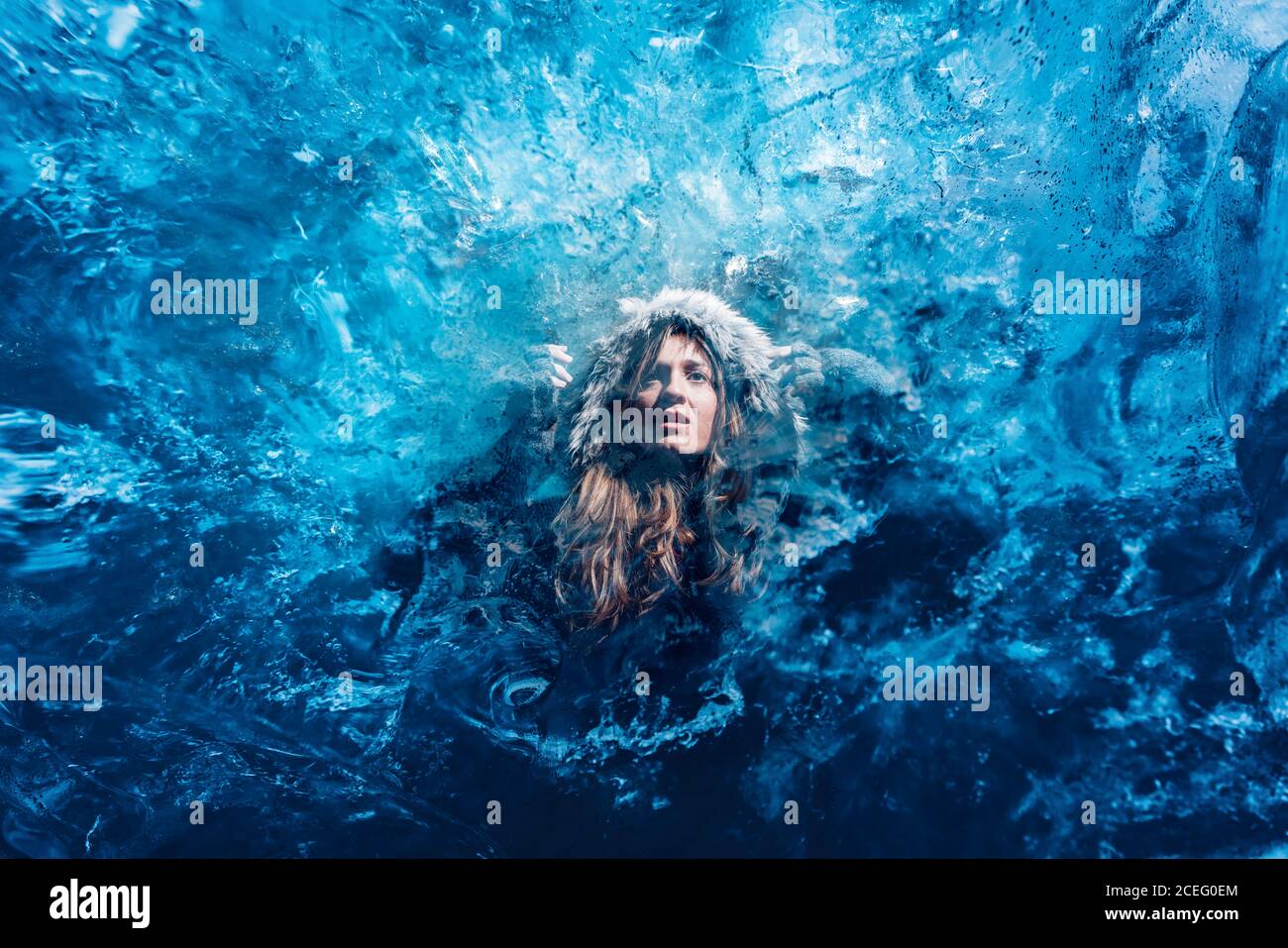 Young sensual Woman in hood standing behind clear blue ice in cave of ...
