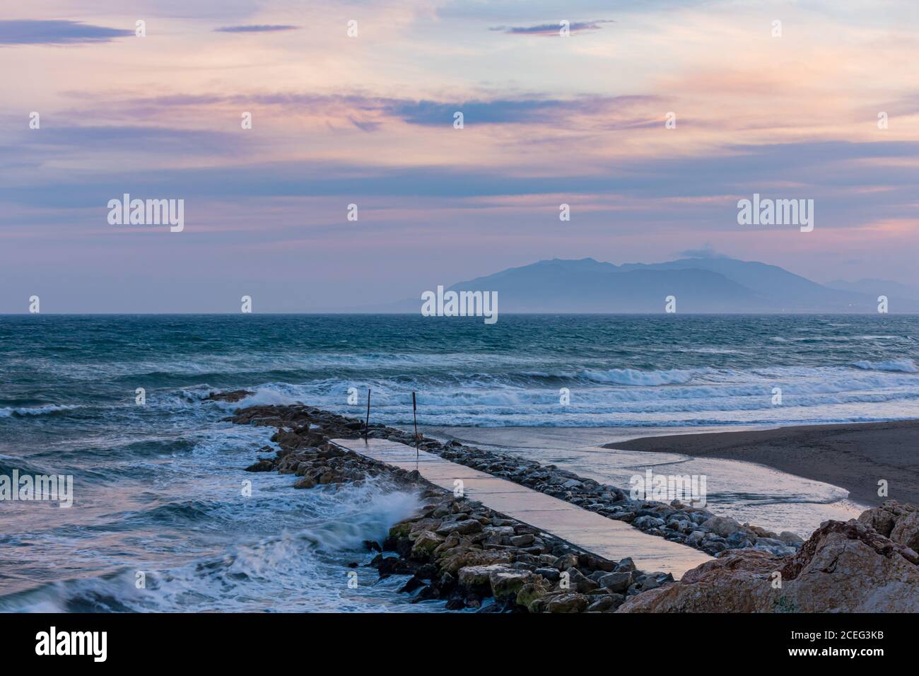 Landscape of a breakwater on a beach with waves, mountains in the ...