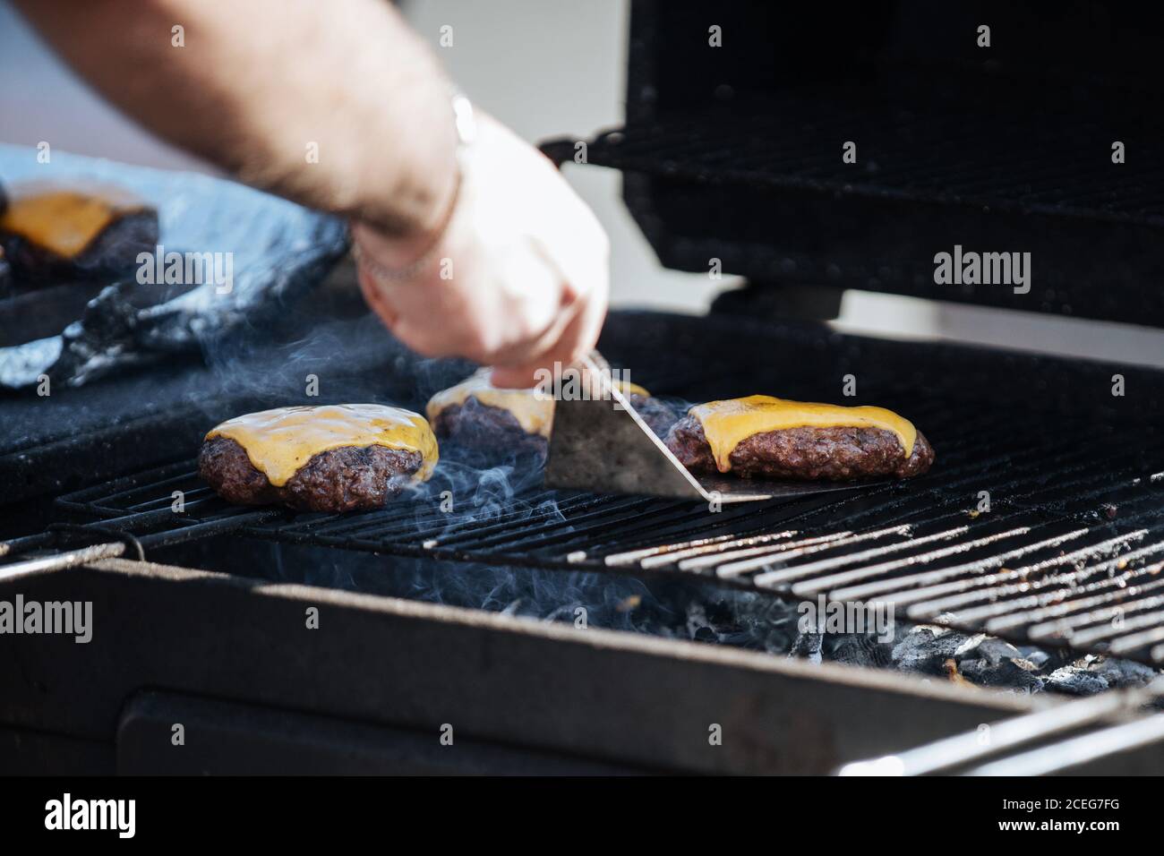 Crop shot of man roasting meat patties with cheese on smoking grill in ...