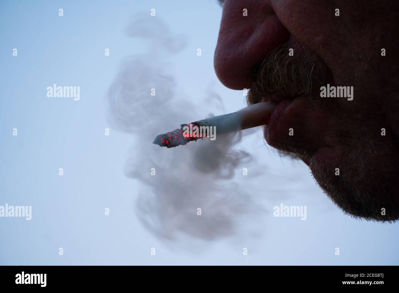 A man with a mustache smokes a cigarette in close-up. Thick smoke from ...
