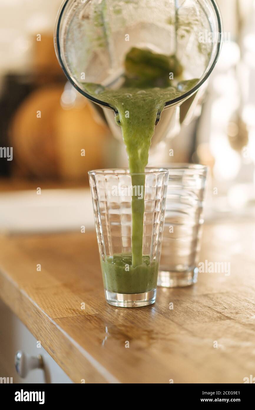 Crop female hand pouring healthy green smoothie from blender cup into ...
