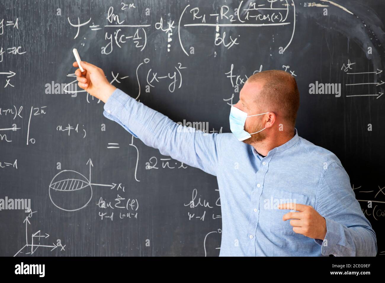 Male teacher with mask teaching math lesson at school. Social ... Male teacher with mask teaching math lesson at school. Social ...