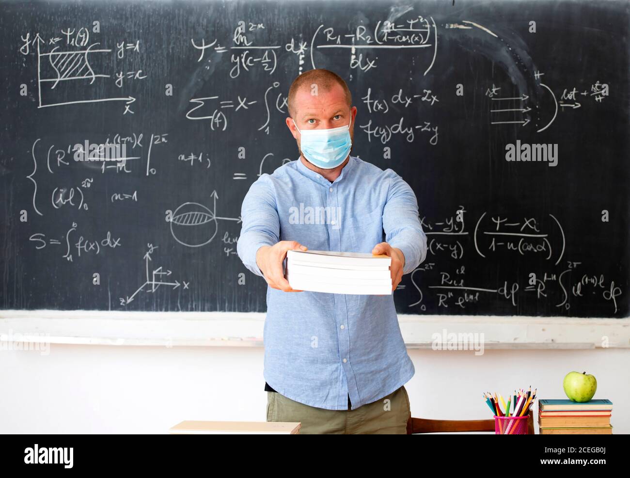 Teacher with face mask welcoming children back at school after lockdown ...
