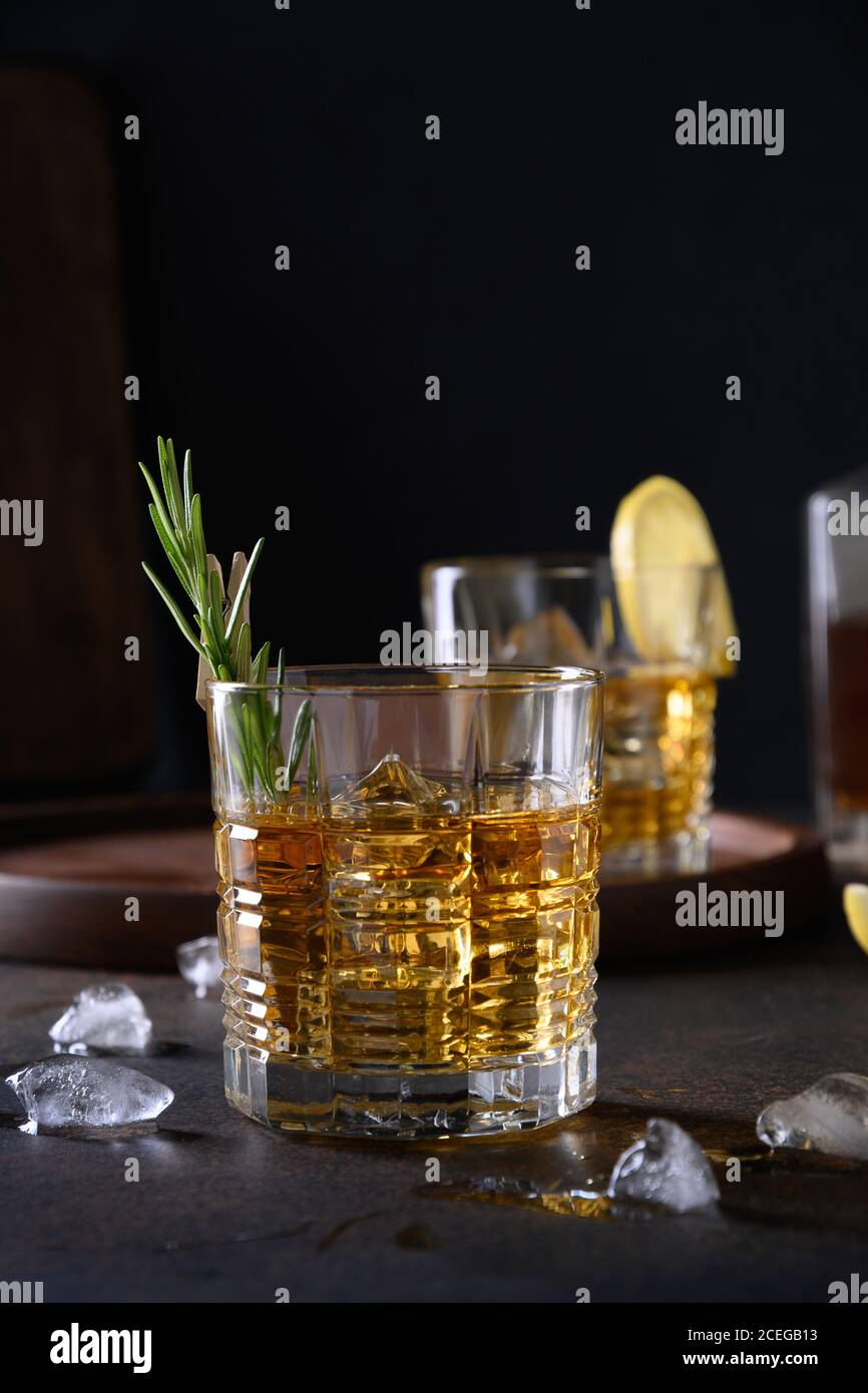 Two glasses of cold whiskey with rosemary, lemon peels on dark brown ...