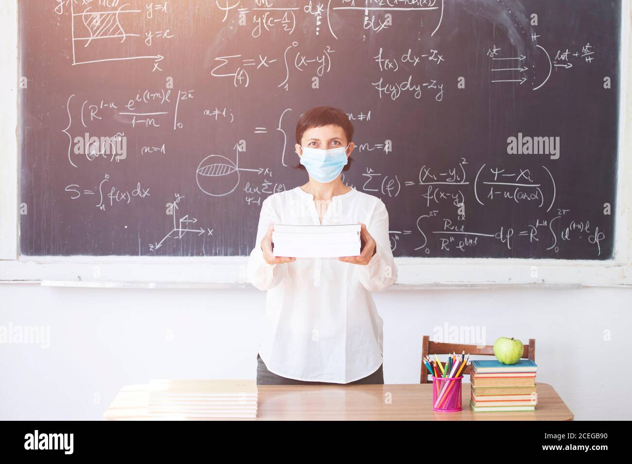 Teacher with face mask welcoming children back at school after lockdown ...