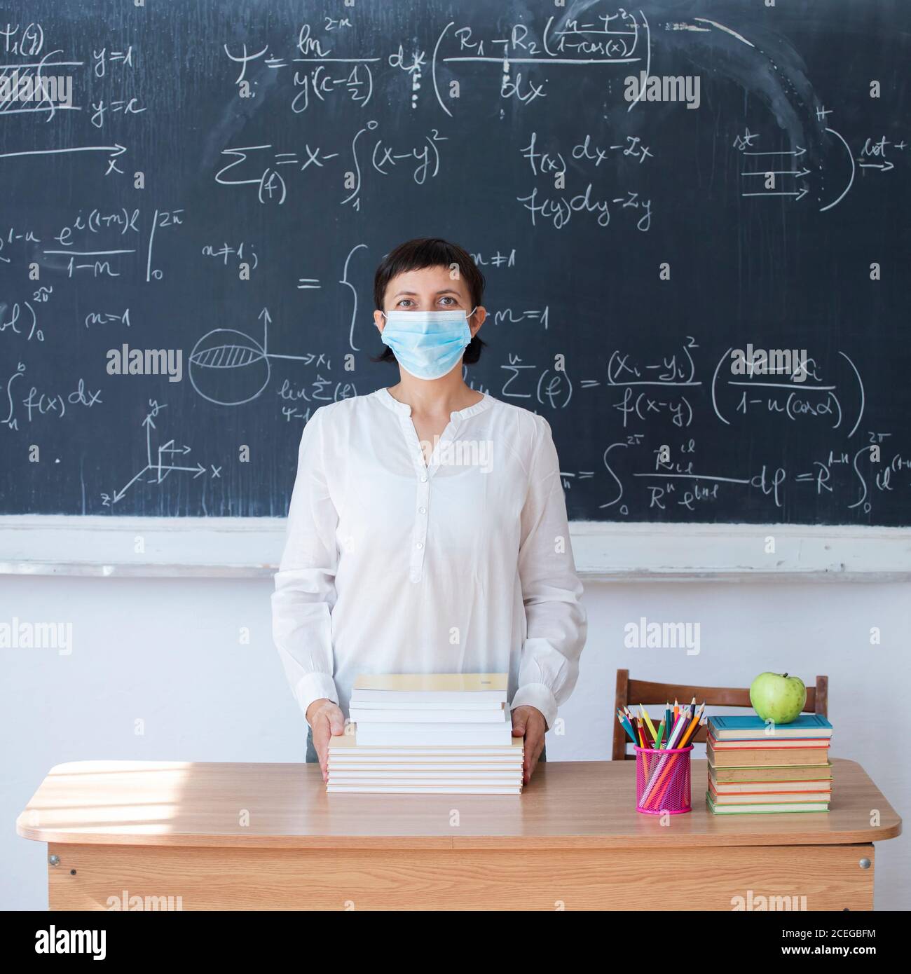 Teacher with face mask welcoming children back at school after lockdown ...
