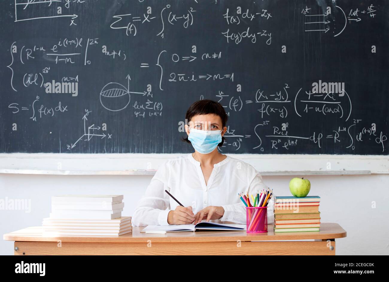 Teacher with face mask welcoming children back at school after lockdown ...