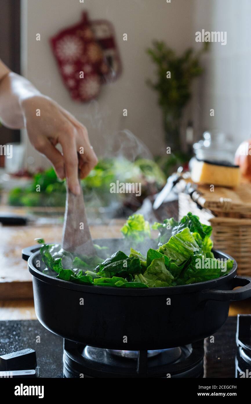 Crop female hand stirring with wooden spatula chopped vegetable leaves ...